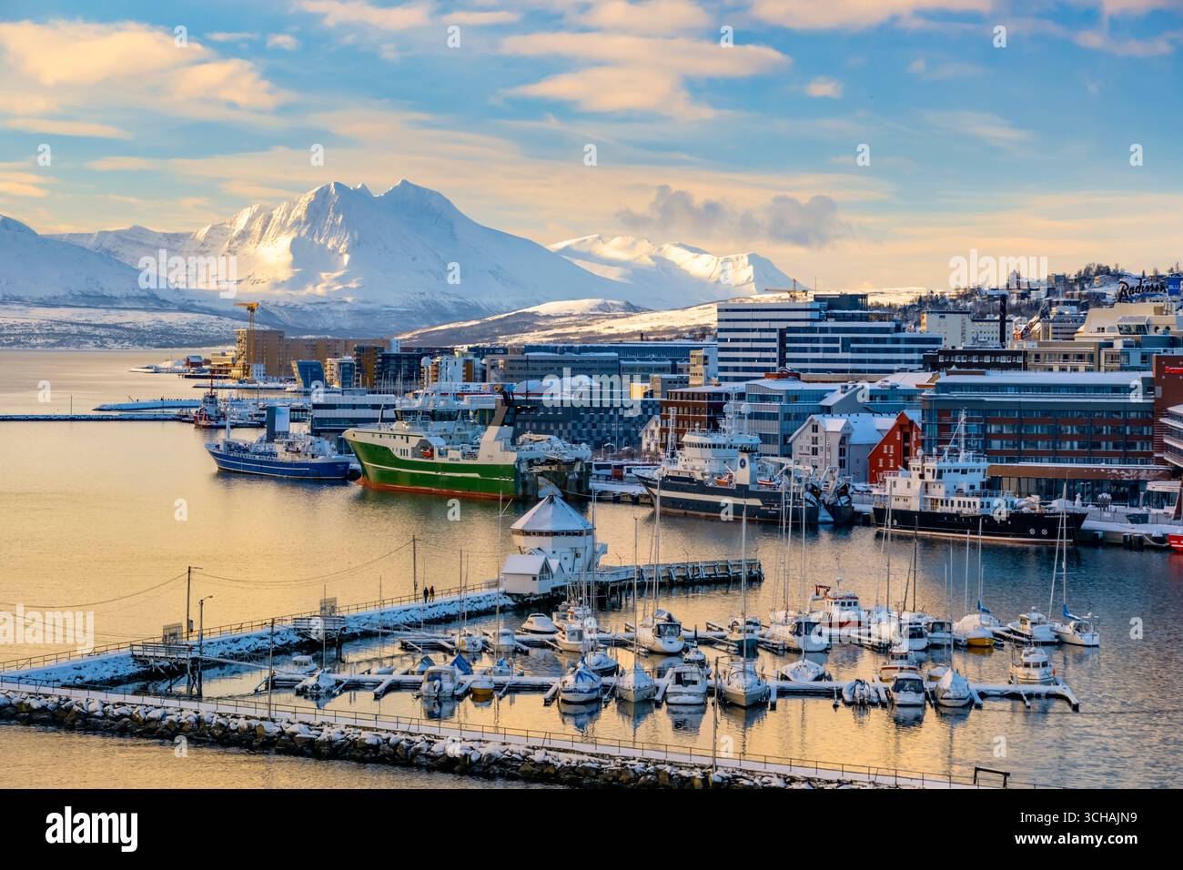 Snow-covered Troms harbor with docked boats and ships, nestled against ...