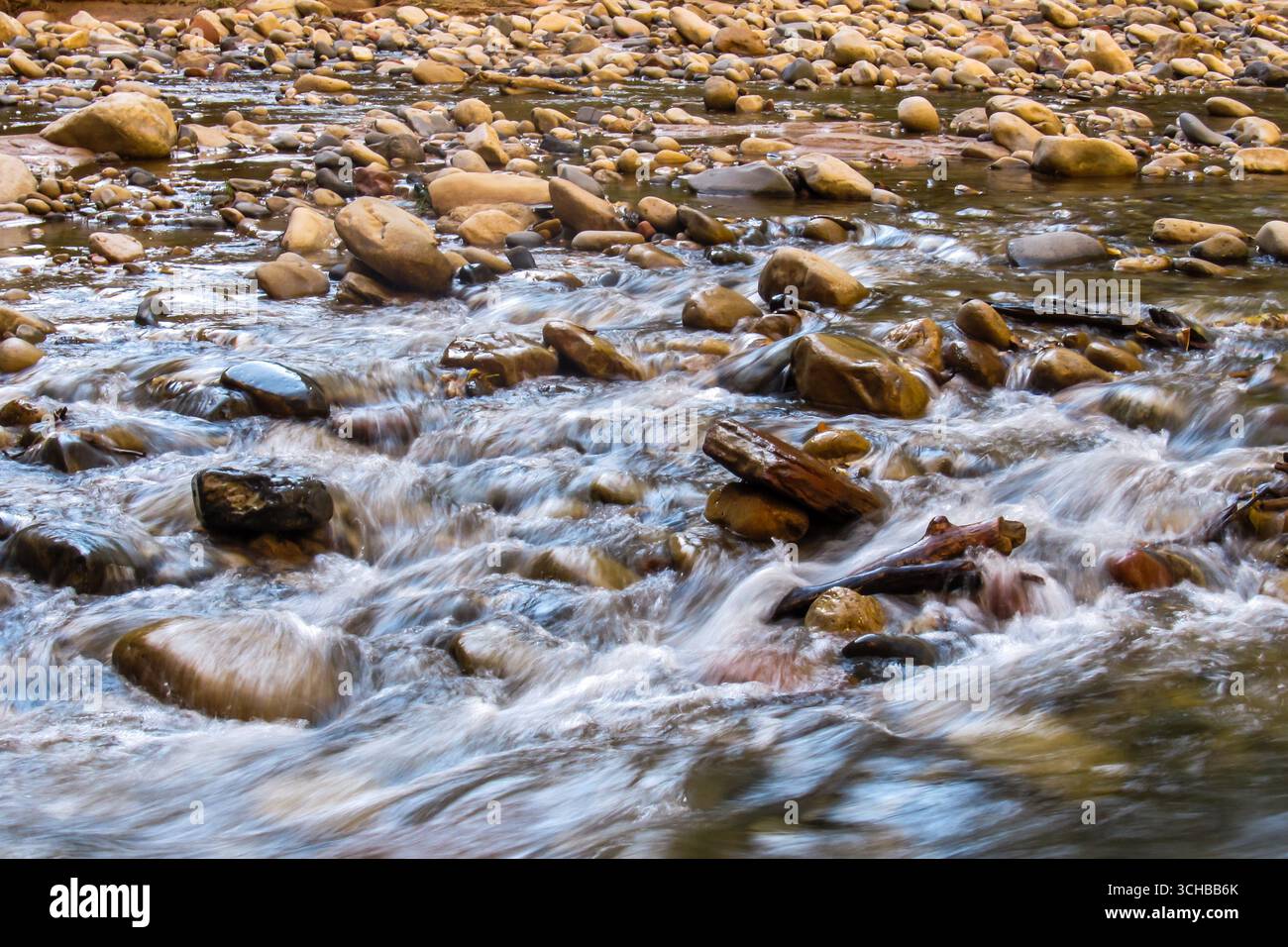 Close-up of fast flowing water over the rounded pebbles in a riverbed ...