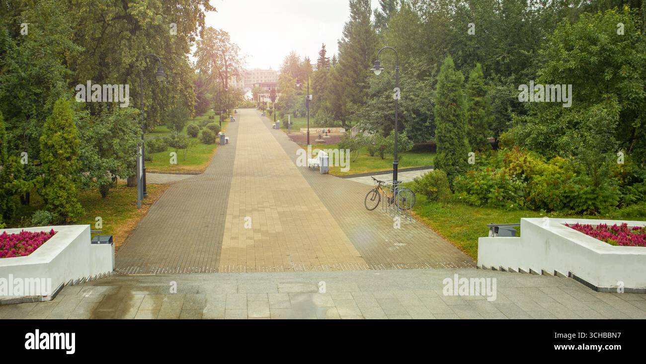 Pedestrian alley in a green city park benches lamps bike rack and ...