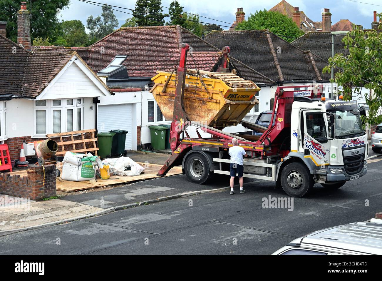 A skip being unloaded by a lorry to a suburban bungalow that is having ...