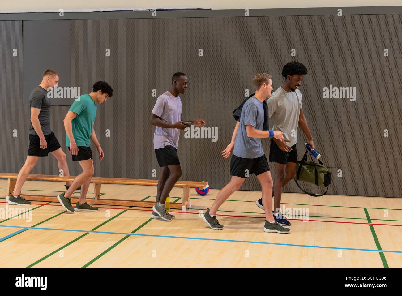 Male teammates walking in gym passing bench with volleyball, carrying ...