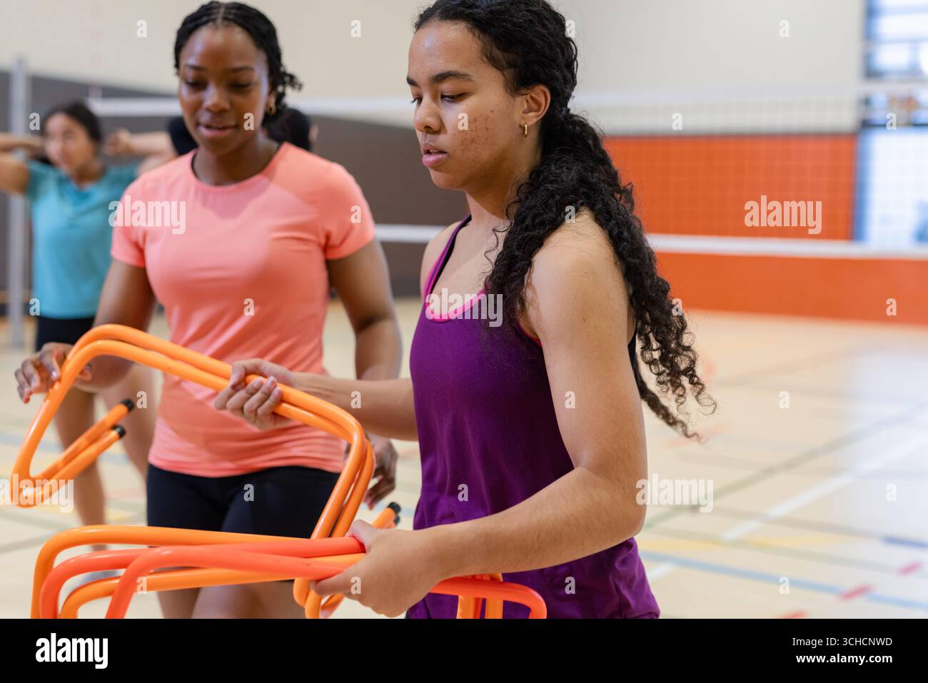 Diverse female teammates arranging orange agility hurdles along painted ...