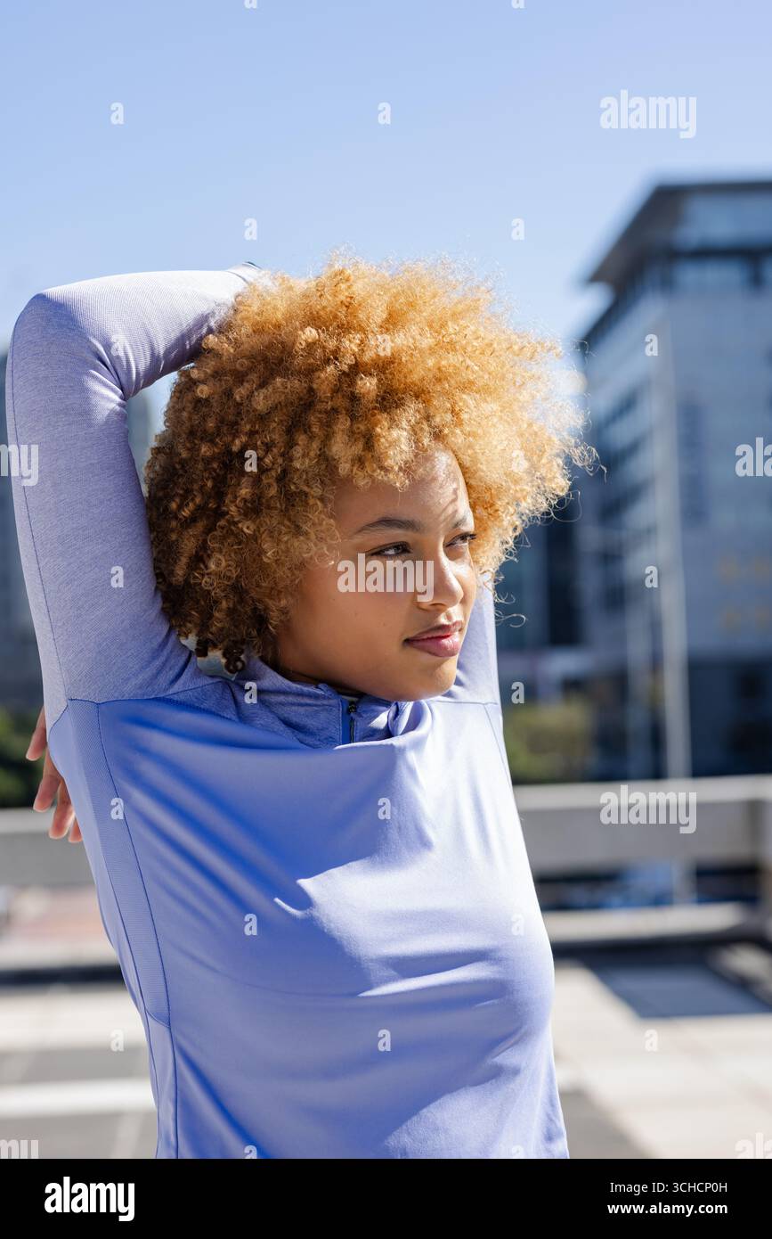 African American woman lifting arms overhead on roof terrace with ...