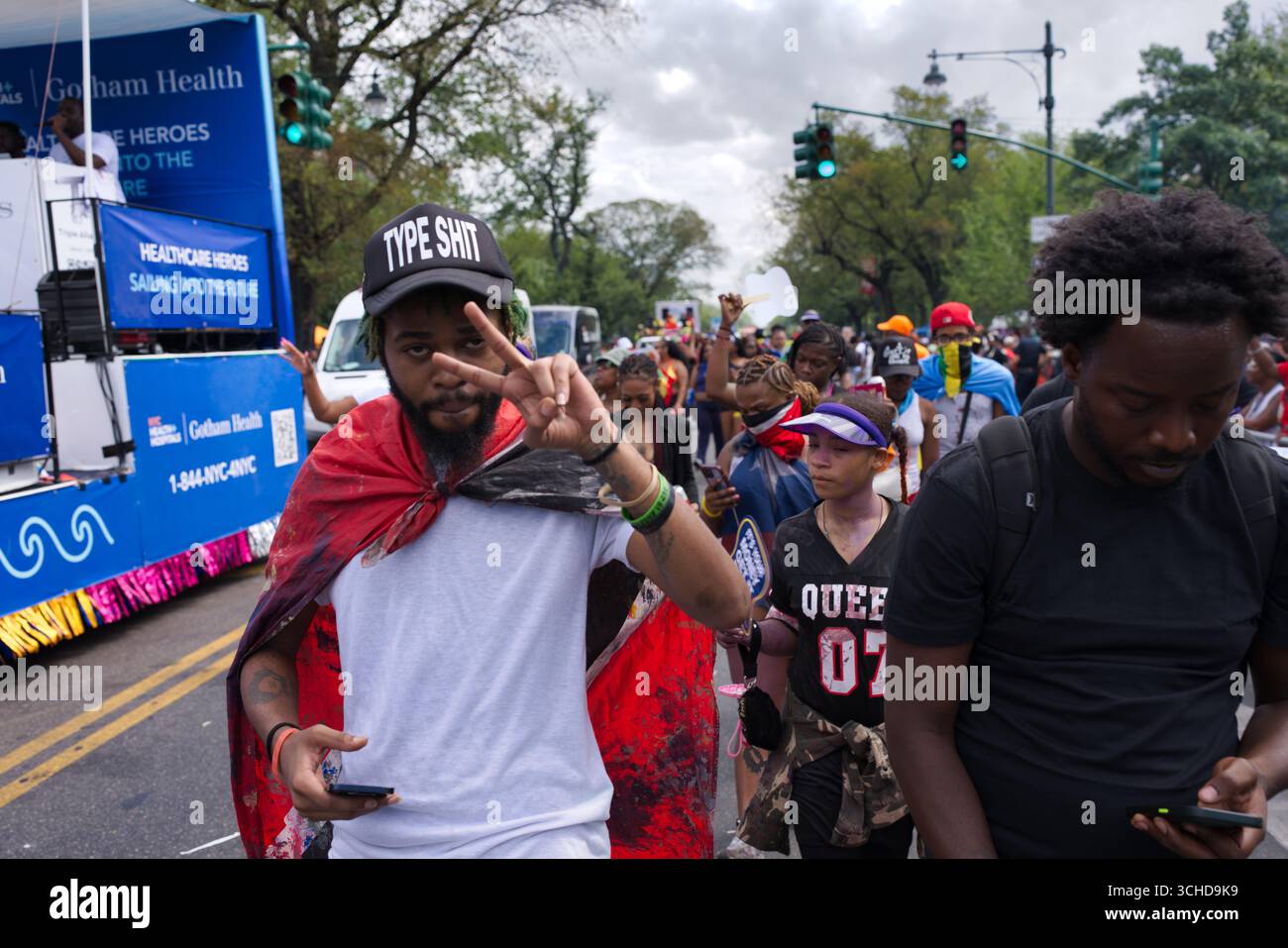 A man in a cape and hat flashes a peace sign while walking in a parade ...