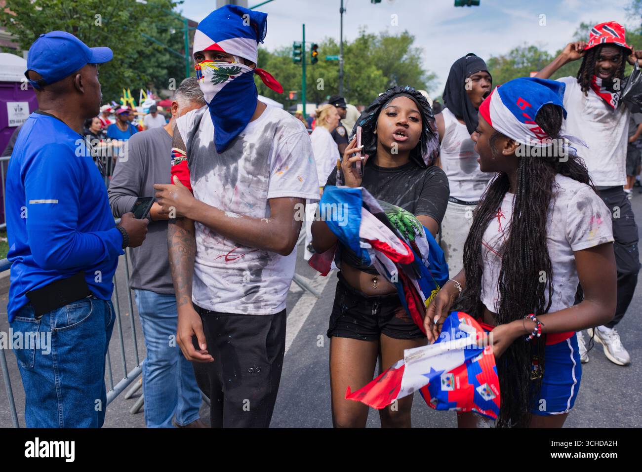 People in colorful attire, some with paint splatters, hold flags at an ...