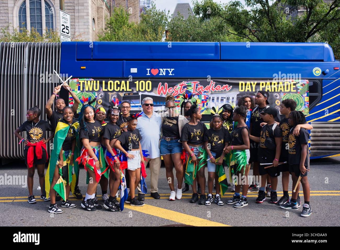 A group of children and adults pose in front of a blue bus adorned with ...