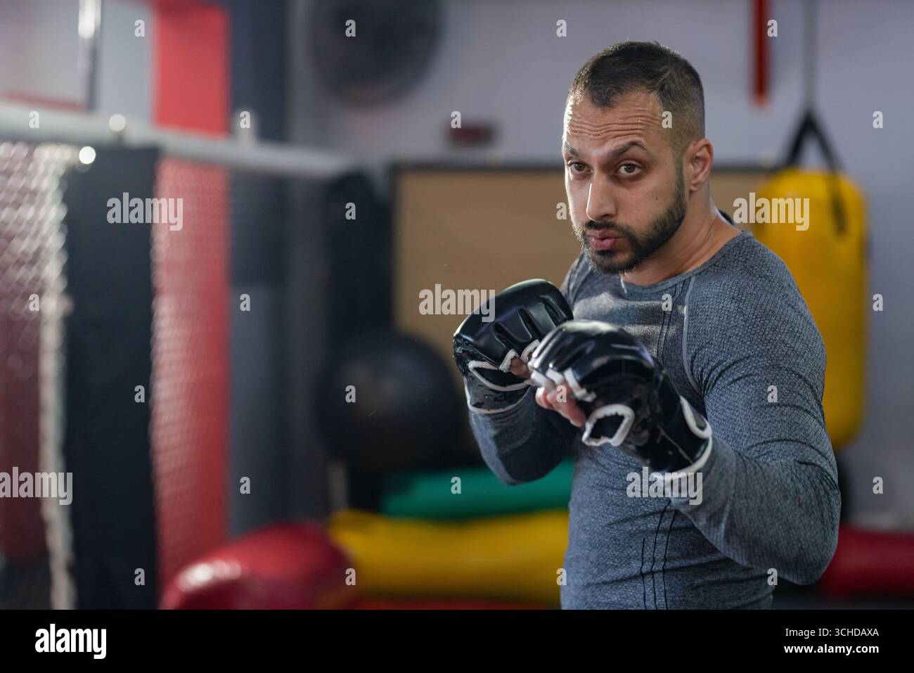Asian indian man standing in martial arts gym holding mma gloves next ...