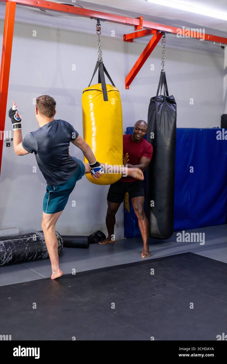 Diverse male partners practicing roundhouse kick on yellow heavy bag at ...