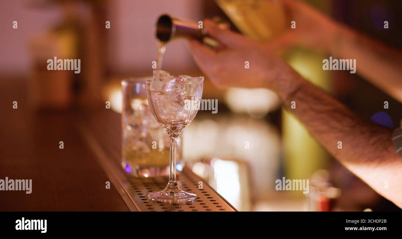 Cocktail making. Using jigger. Barman hand pouring yellow liquid for chilled alcoholic drink ...