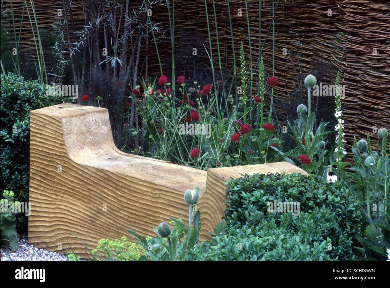 A handcrafted wooden bench rests among lush greenery and colorful ...