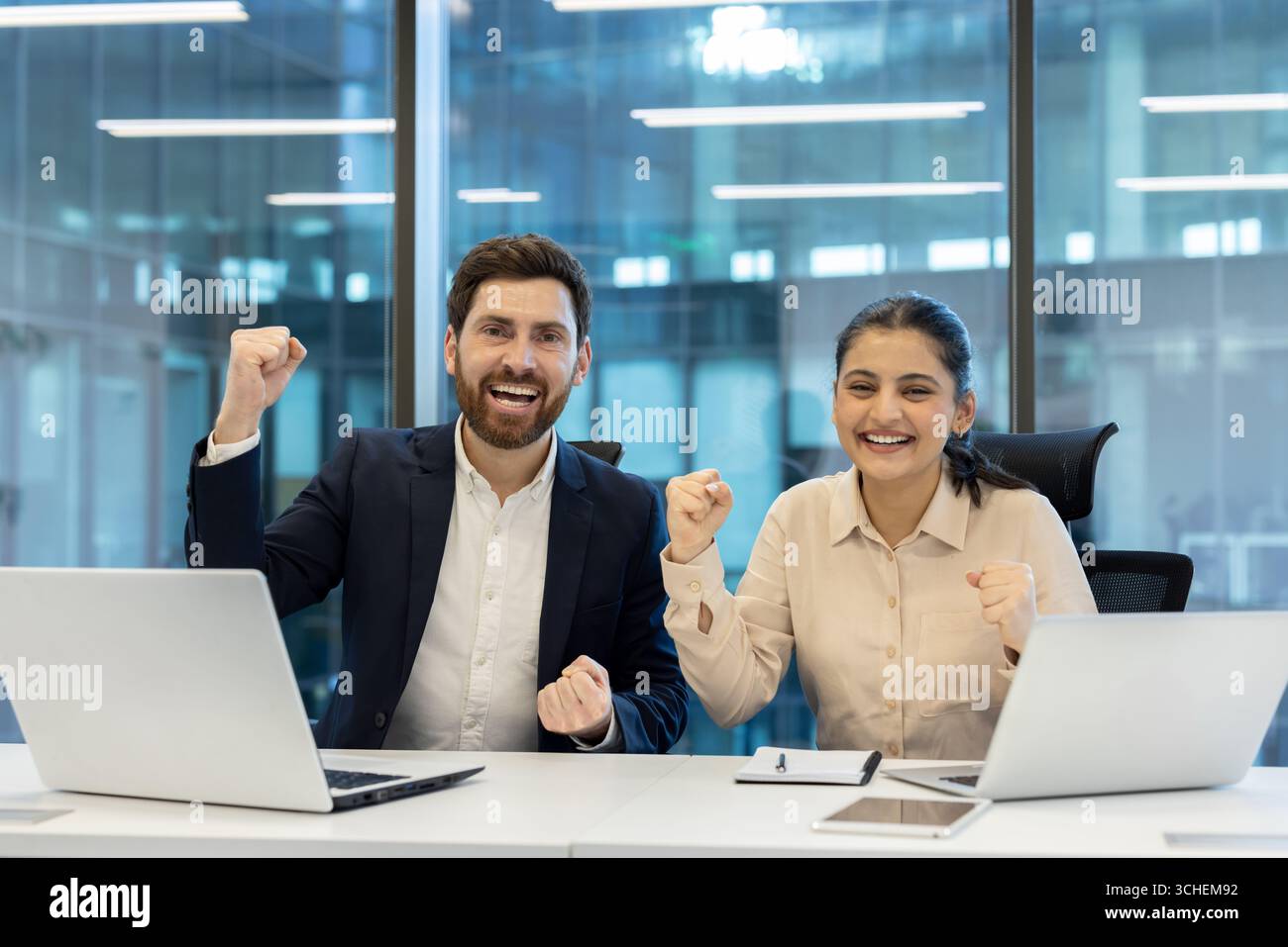 Two happy business colleagues are raising their fists in a modern ...