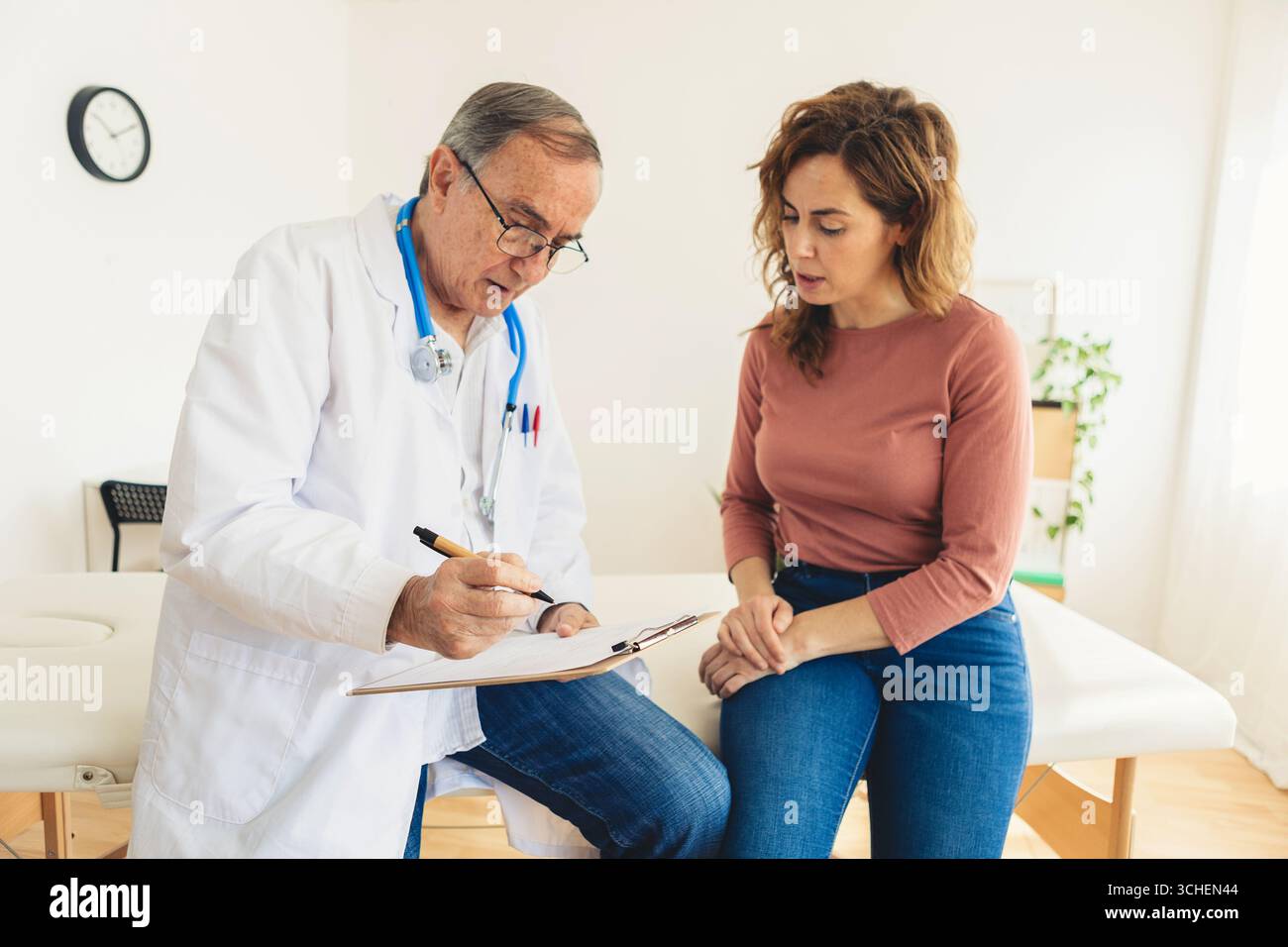 Senior doctor taking notes while talking with a patient in the medical ...