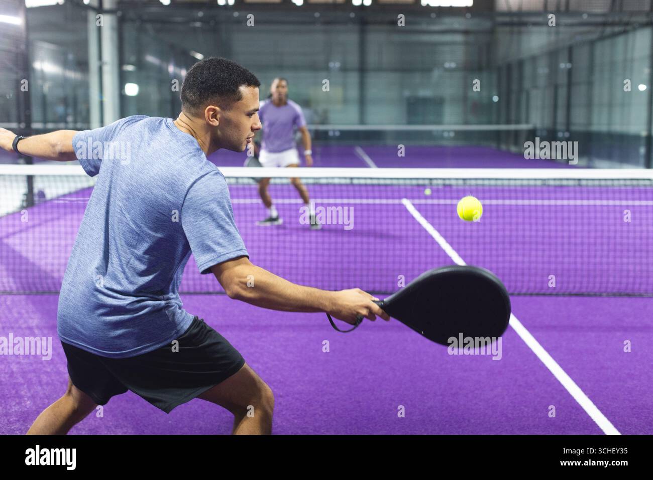 African american male opponents hitting yellow pickleball with black ...