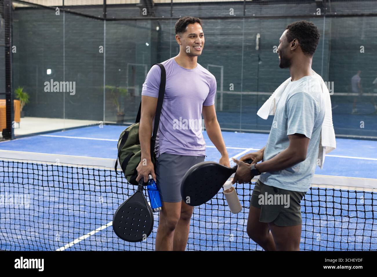 Diverse male friends chatting on padel court at sports club with padel ...