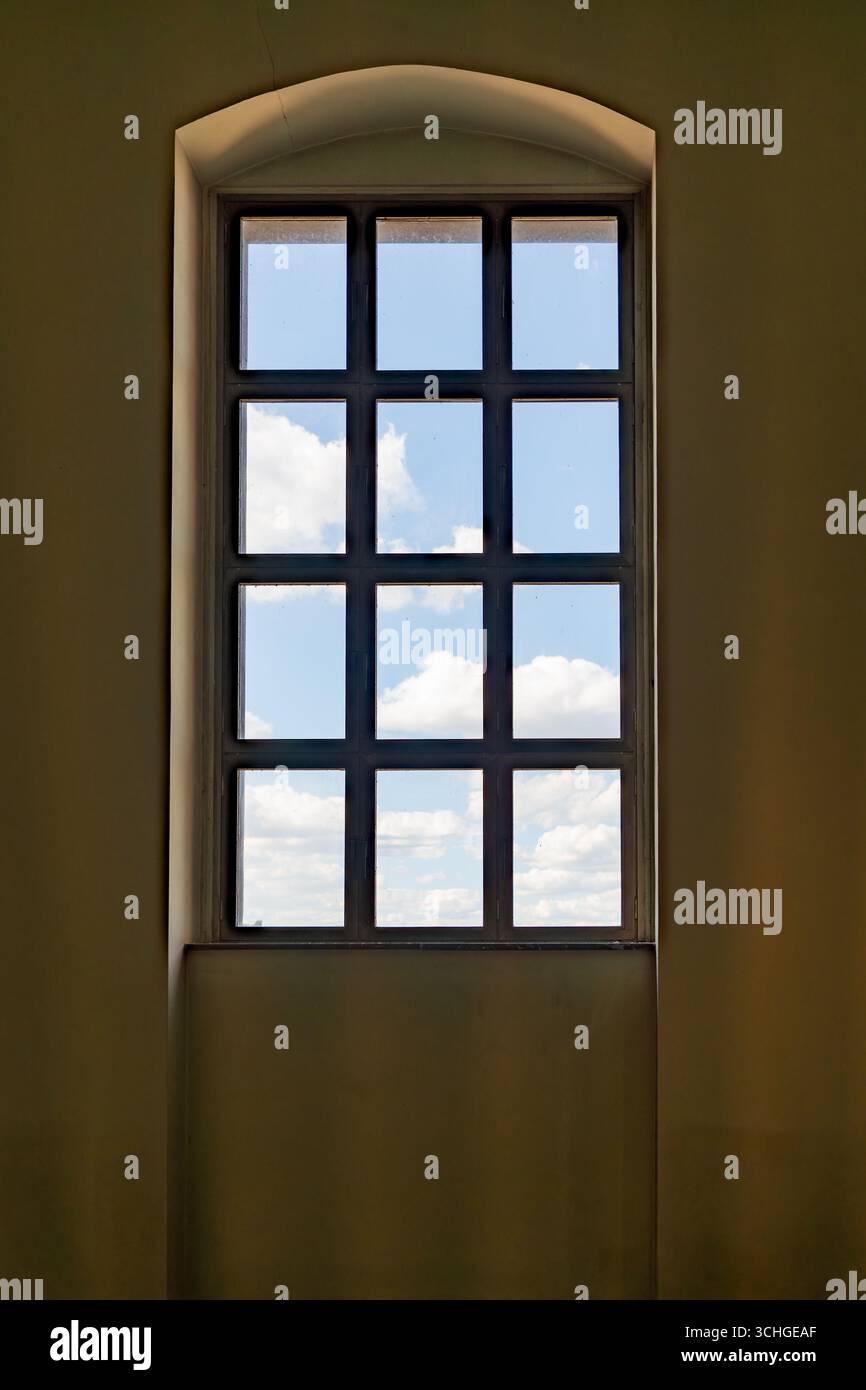 A tall arched window with divided panes shows a clear blue sky and soft ...