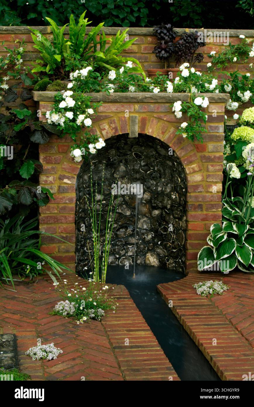 A tranquil garden features a brick fountain surrounded by vibrant ...