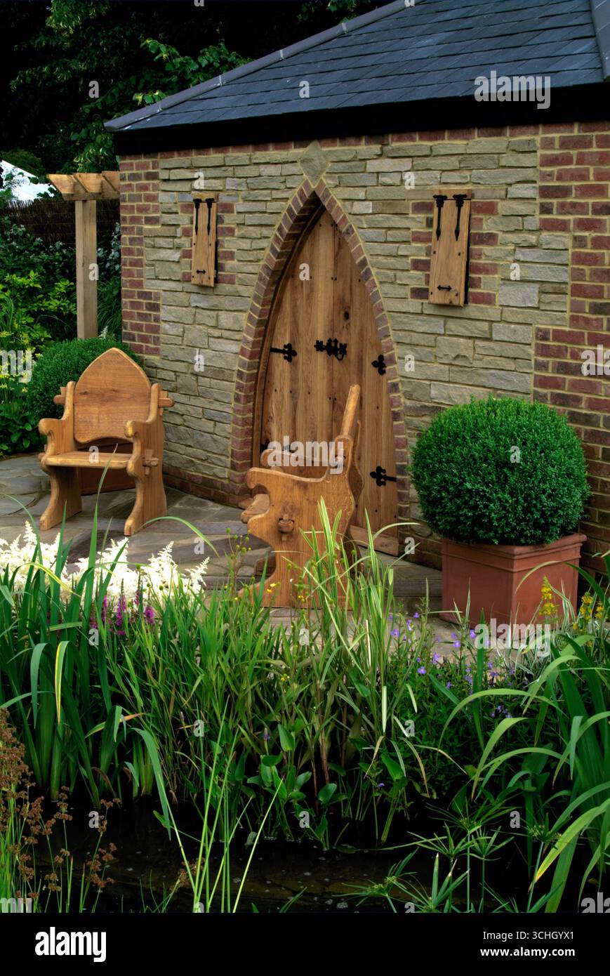 Two rustic wooden chairs sit near a garden shed featuring a stone wall ...