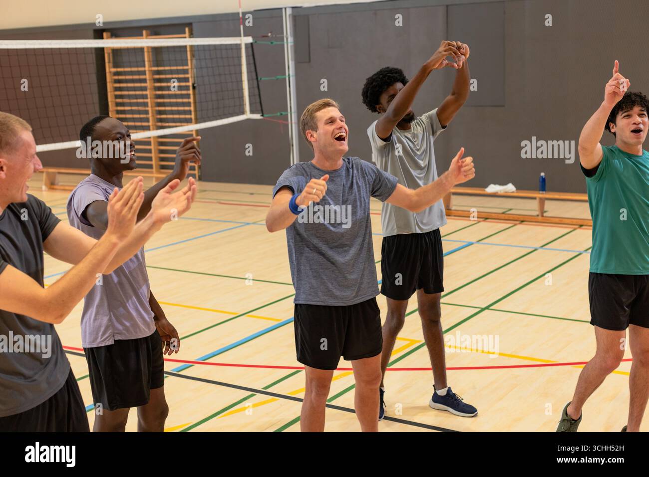 Diverse male volleyball team clapping, raising arms on gym court under ...
