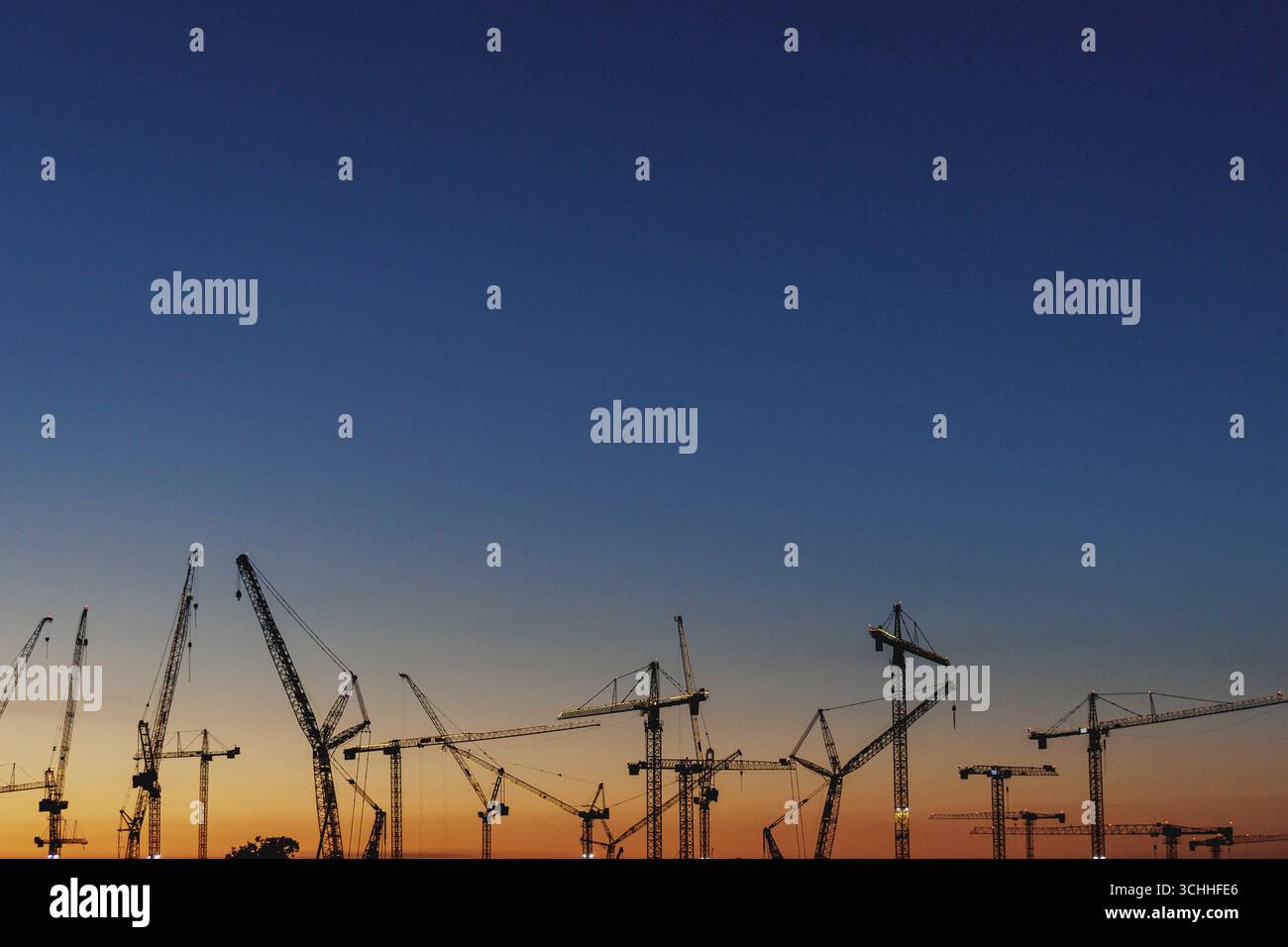 Cranes stand out in the evening light at the construction site of the ...