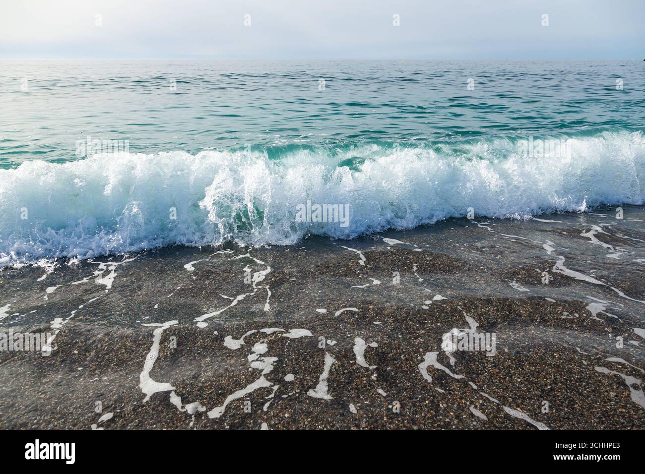 Surf of the sea wave with clear water on the coast with small stones ...