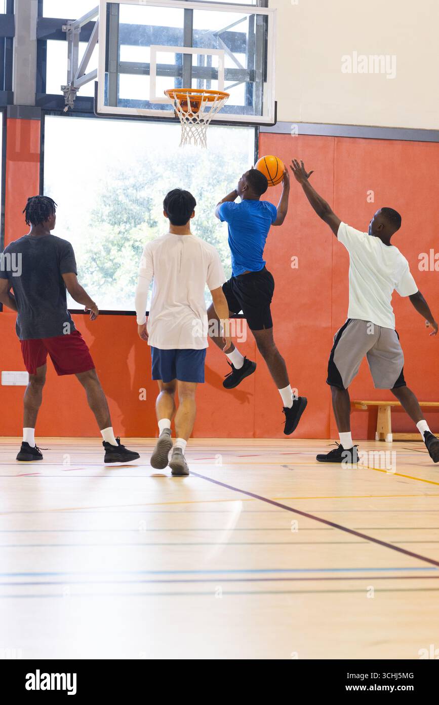 Diverse male friends playing basketball under hoop on wooden court with ...