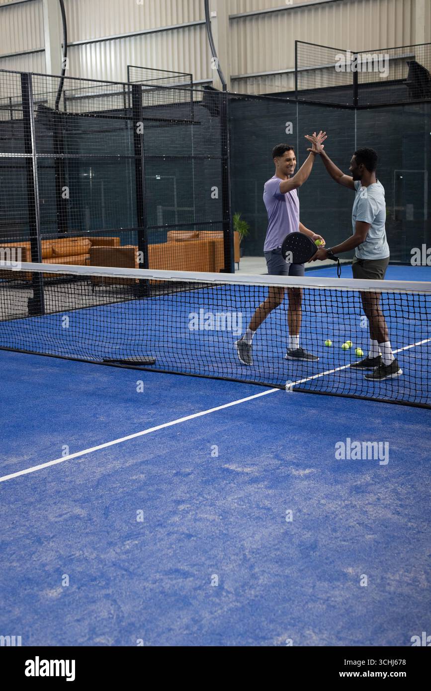 Diverse male friends practicing padel on blue court at sports arena ...