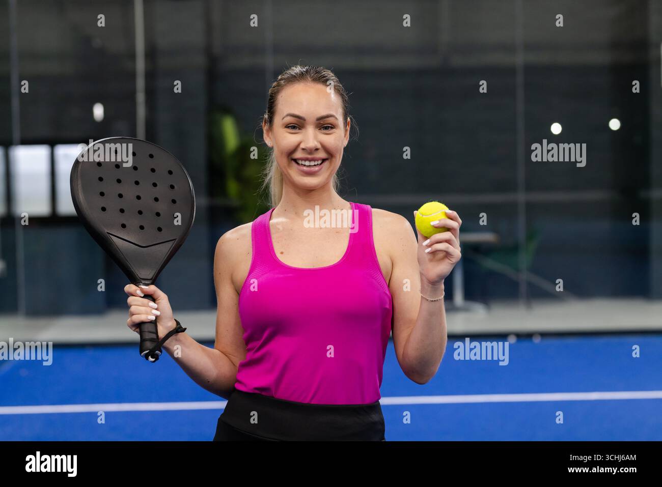 Woman standing on blue padel court in pink top, black skirt, holding ...