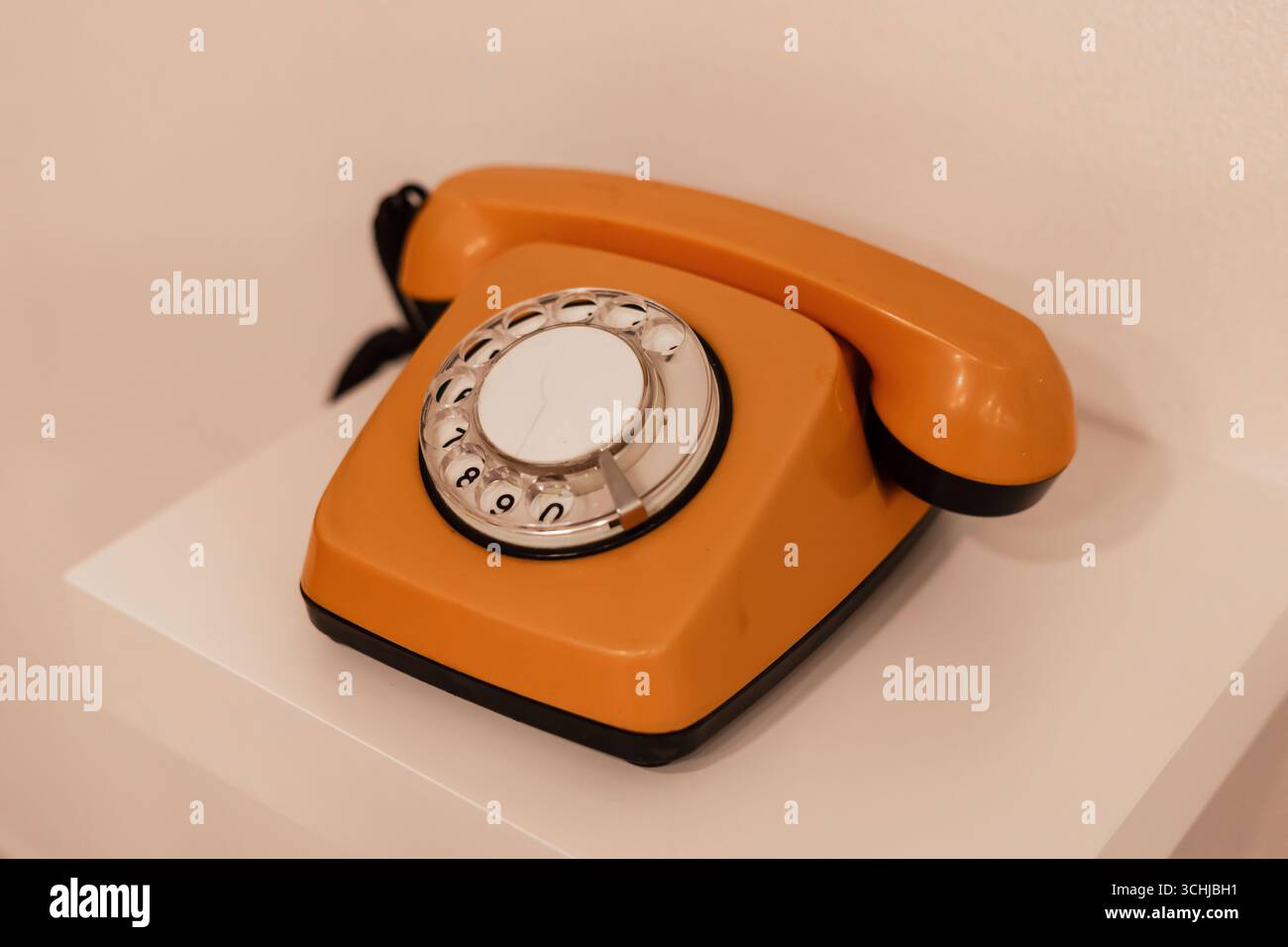 A vintage orange rotary phone is prominently displayed on a sleek ...