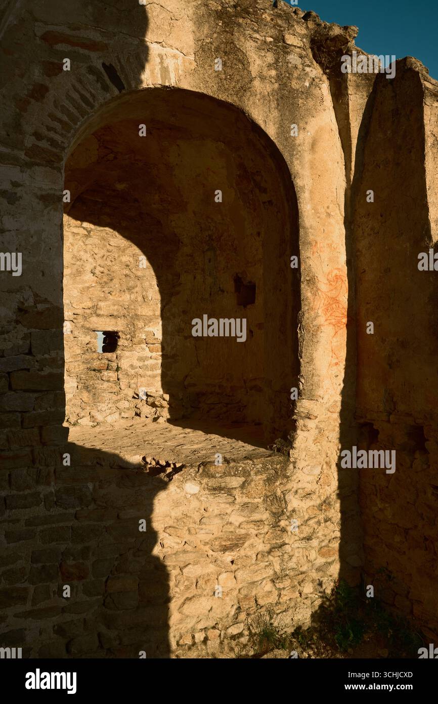 Stone wall of medieval ruined castle with arched opening, sunlit on a ...