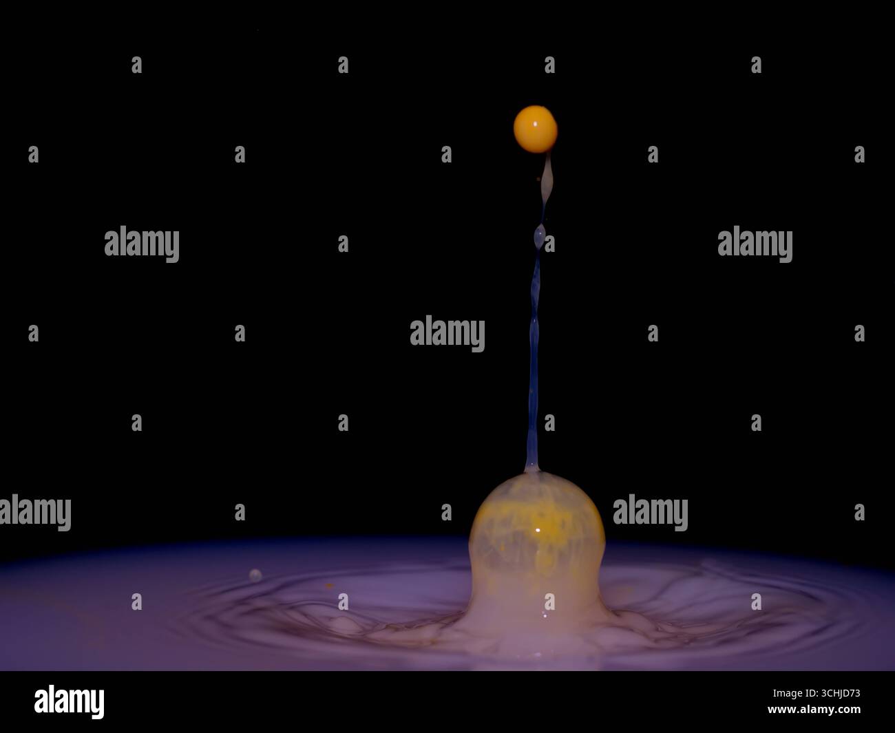 Tall liquid jet rises from a droplet impact with a yellow bead at the ...