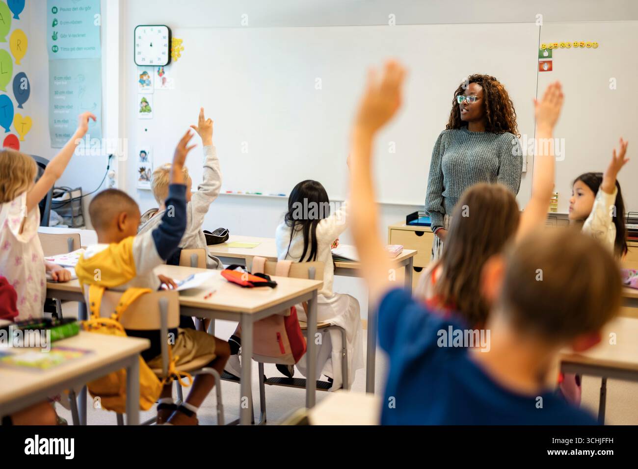 Female teacher asking questions to students sitting with hand raised in ...