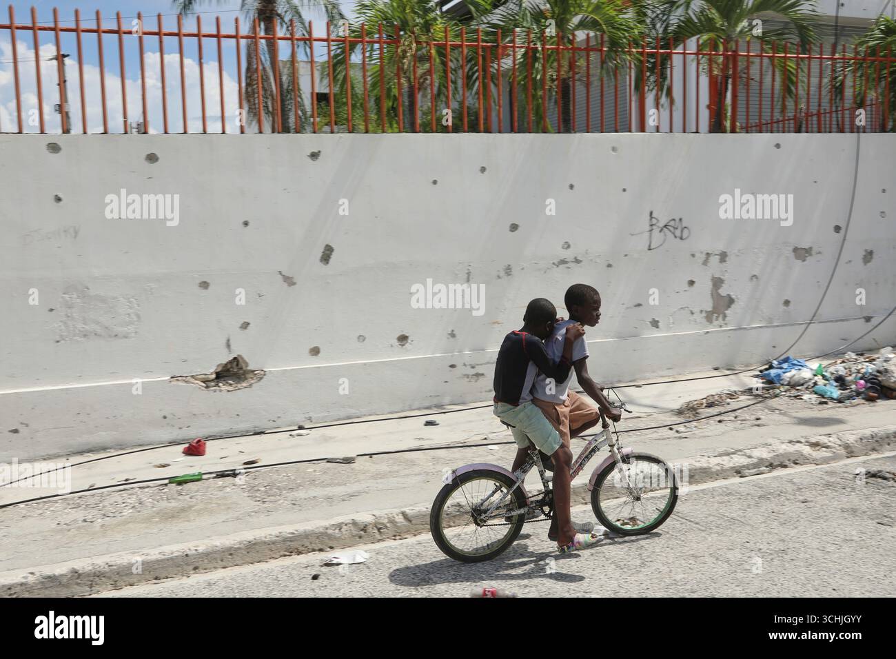 Children ride bicycles past a wall riddled with bullet holes in the ...