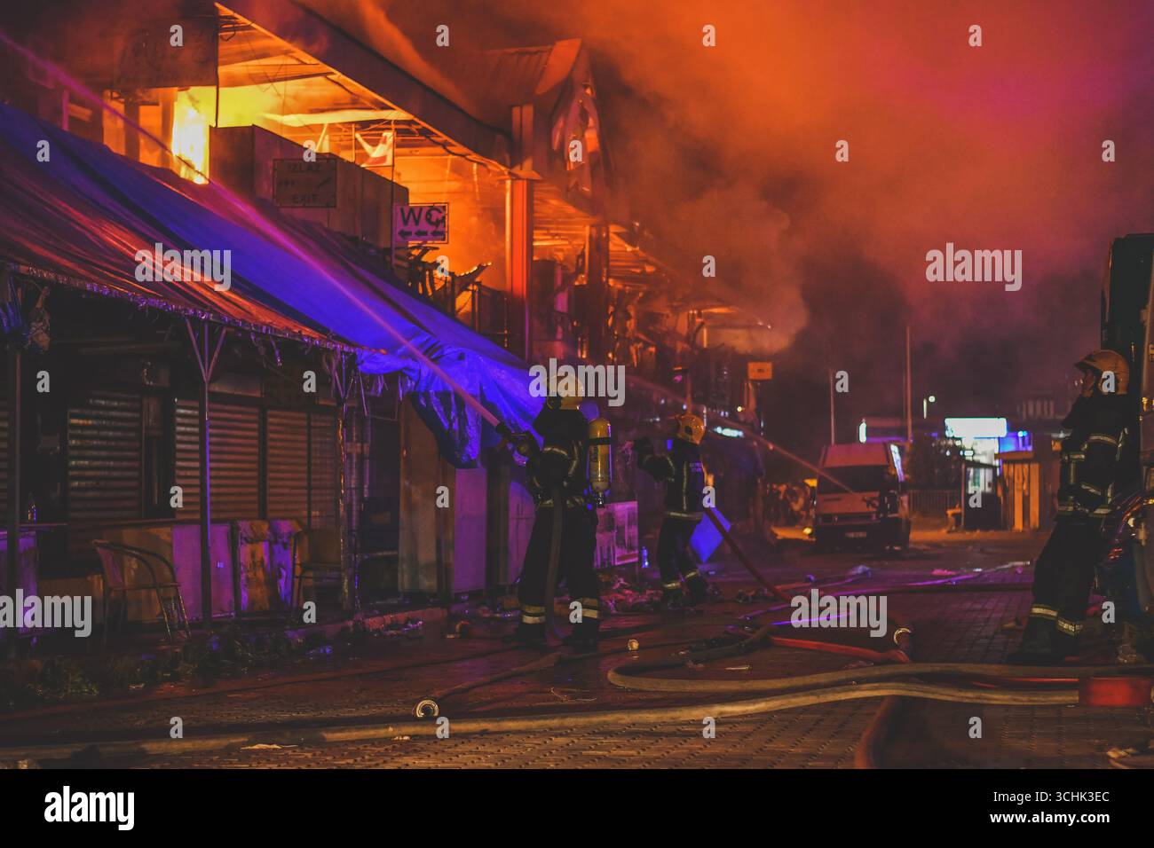 Firefighters in full gear extinguishing a large blaze. Thick smoke and ...