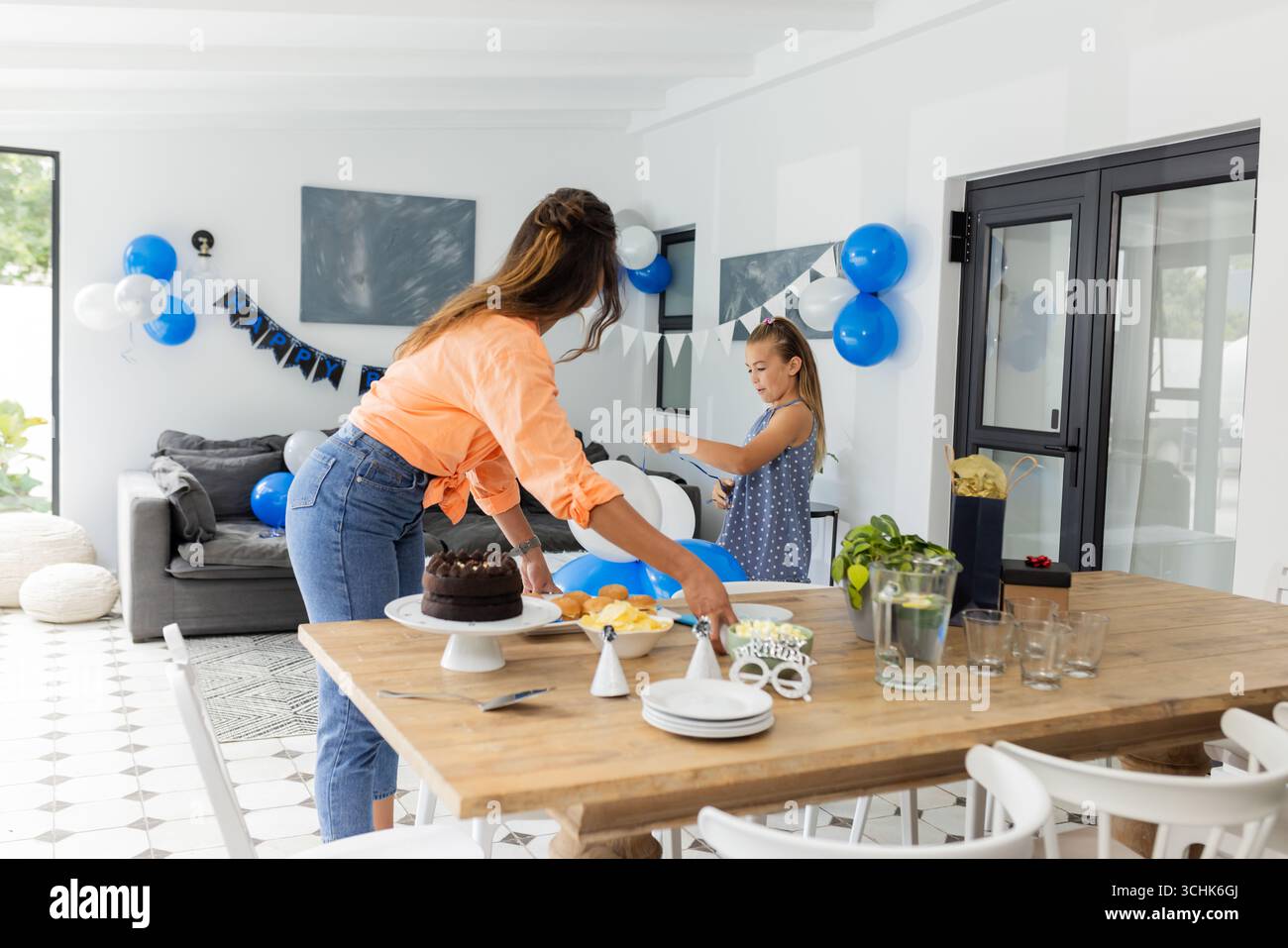 Mother and daughter preparing birthday party table with cake and ...