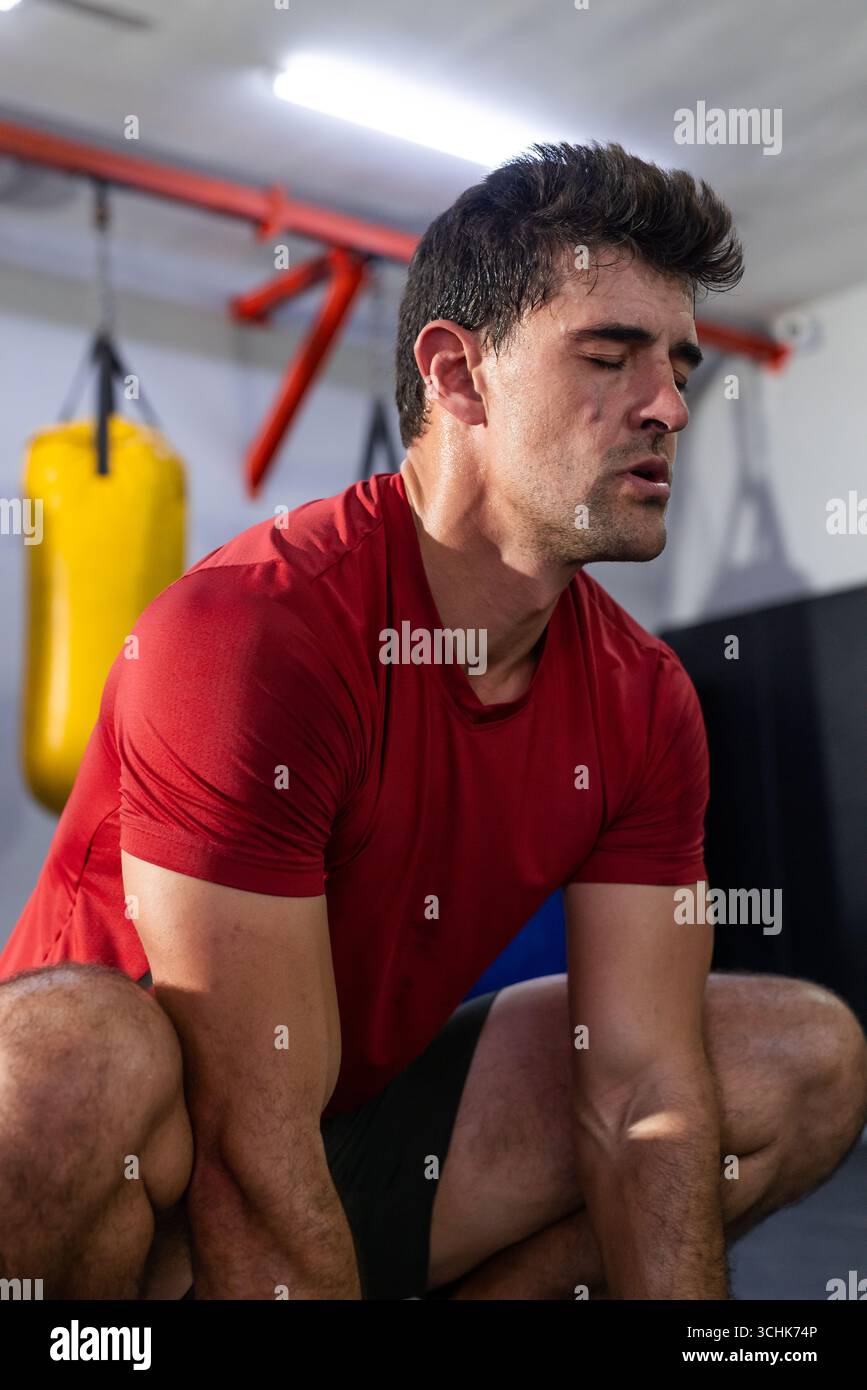 Fit mid-adult male squatting in fitness studio beneath fluorescent ...