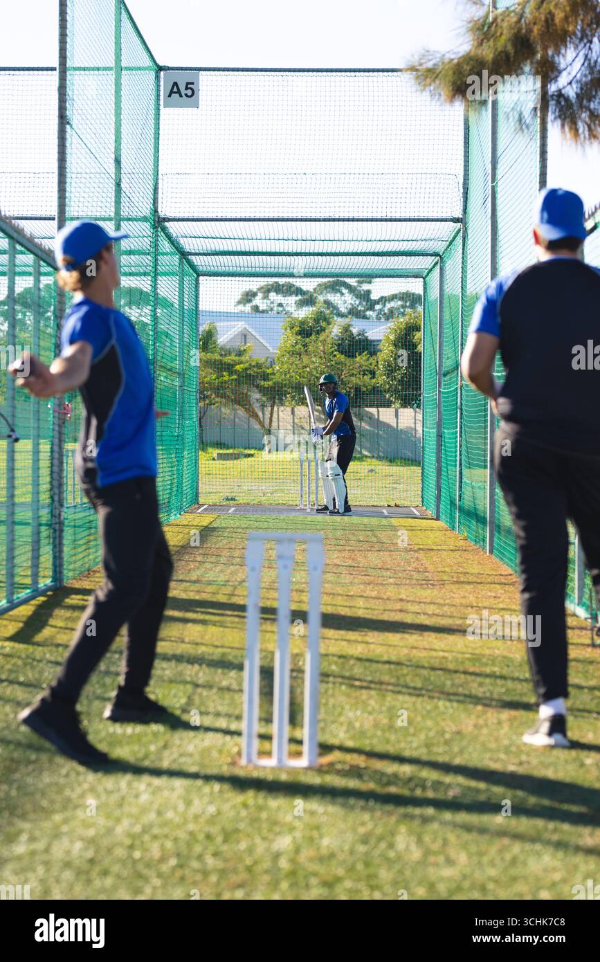 Diverse male teammates practicing cricket in net tunnel with batsman in ...