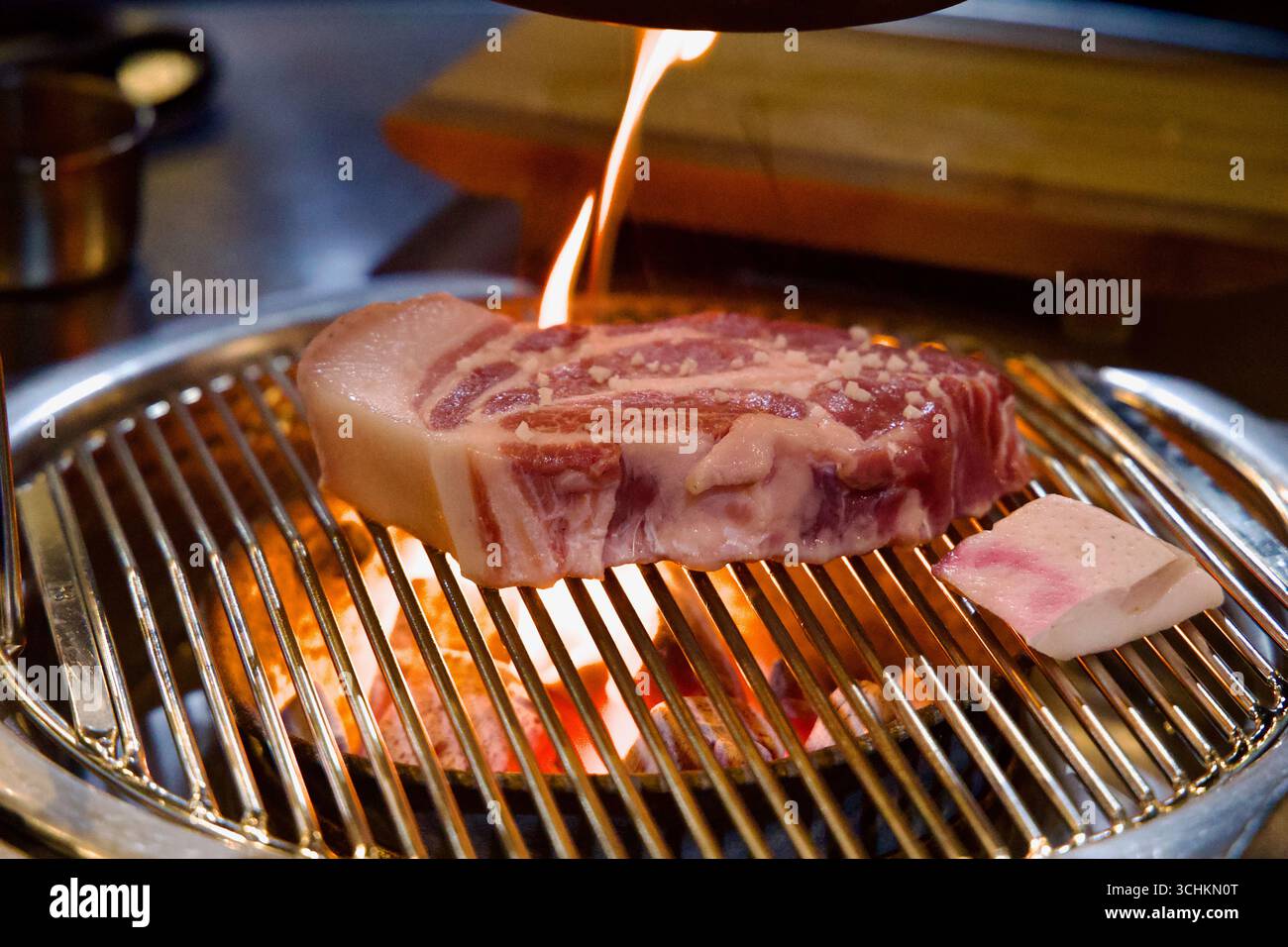 A short flare of fire licks the Jeju black pork as it cooks on a ...