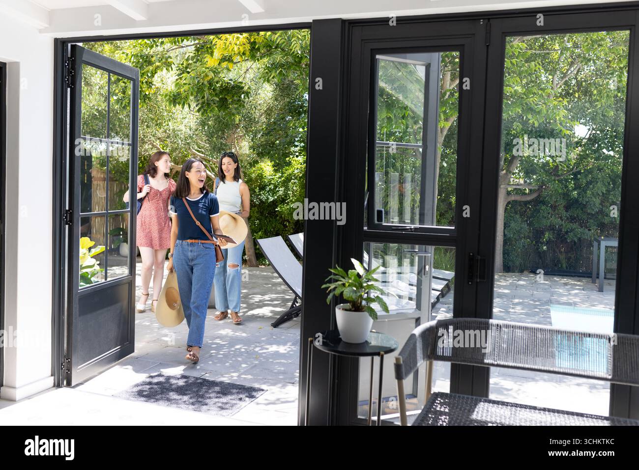 Walking through open doors, three young women enter sunlit patio area ...