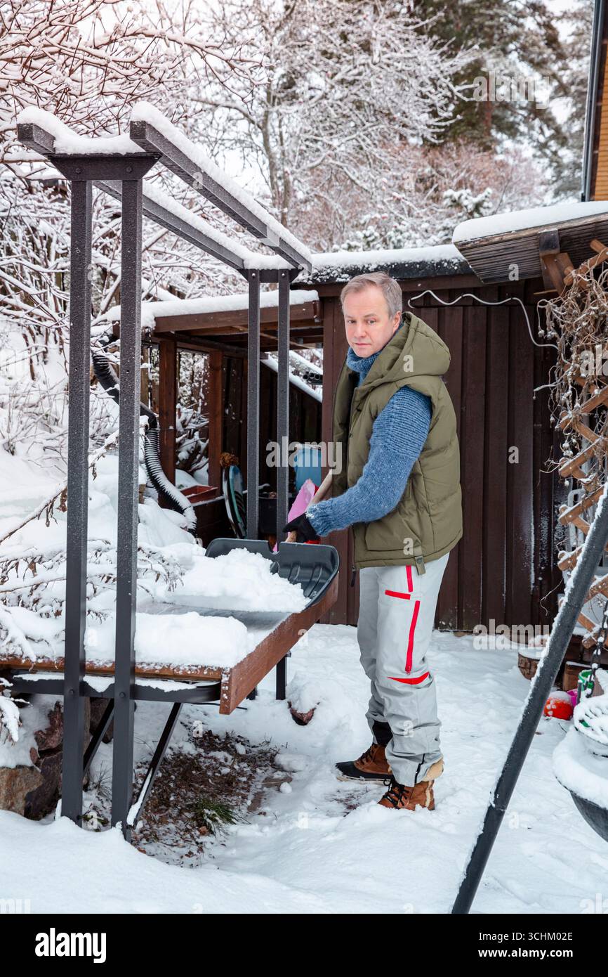 Man shoveling snow in backyard on a wintry morning, bundled in warm ...