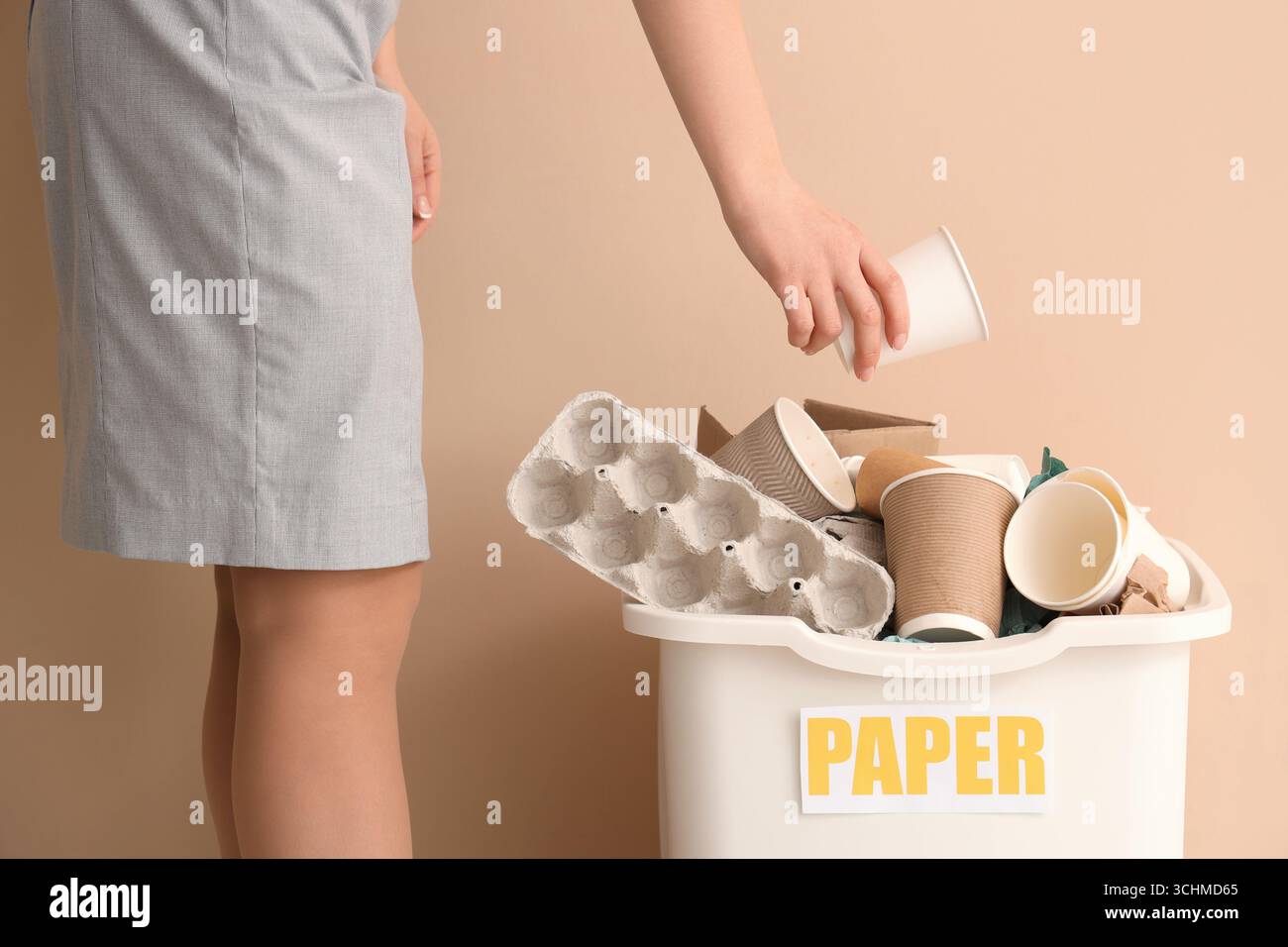 Woman throwing litter in recycling bin with paper near beige wall ...