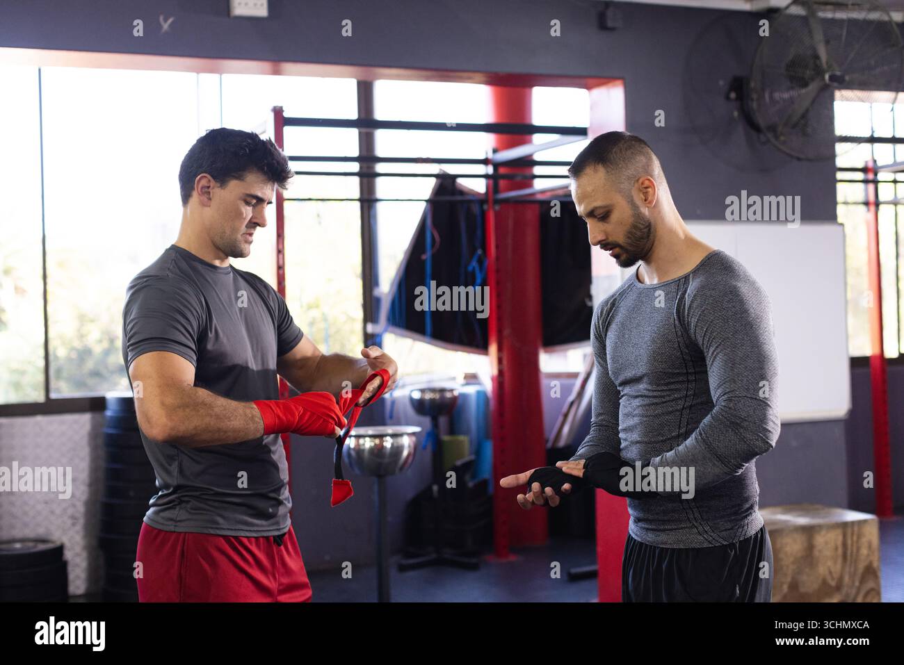 Diverse male training partners wrapping hand wraps at gym with window ...