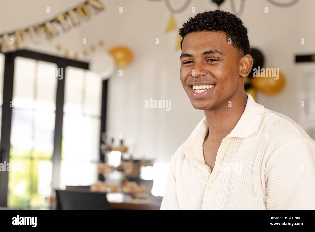 Smiling young man celebrating graduation at home with party decorations ...