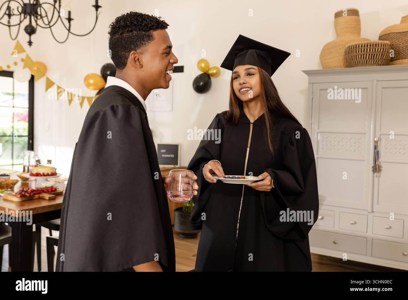 Diverse graduates in caps and gowns celebrating with food and drinks at ...