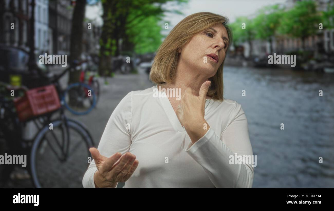 Middle aged caucasian woman fans air with hands on street under canal ...