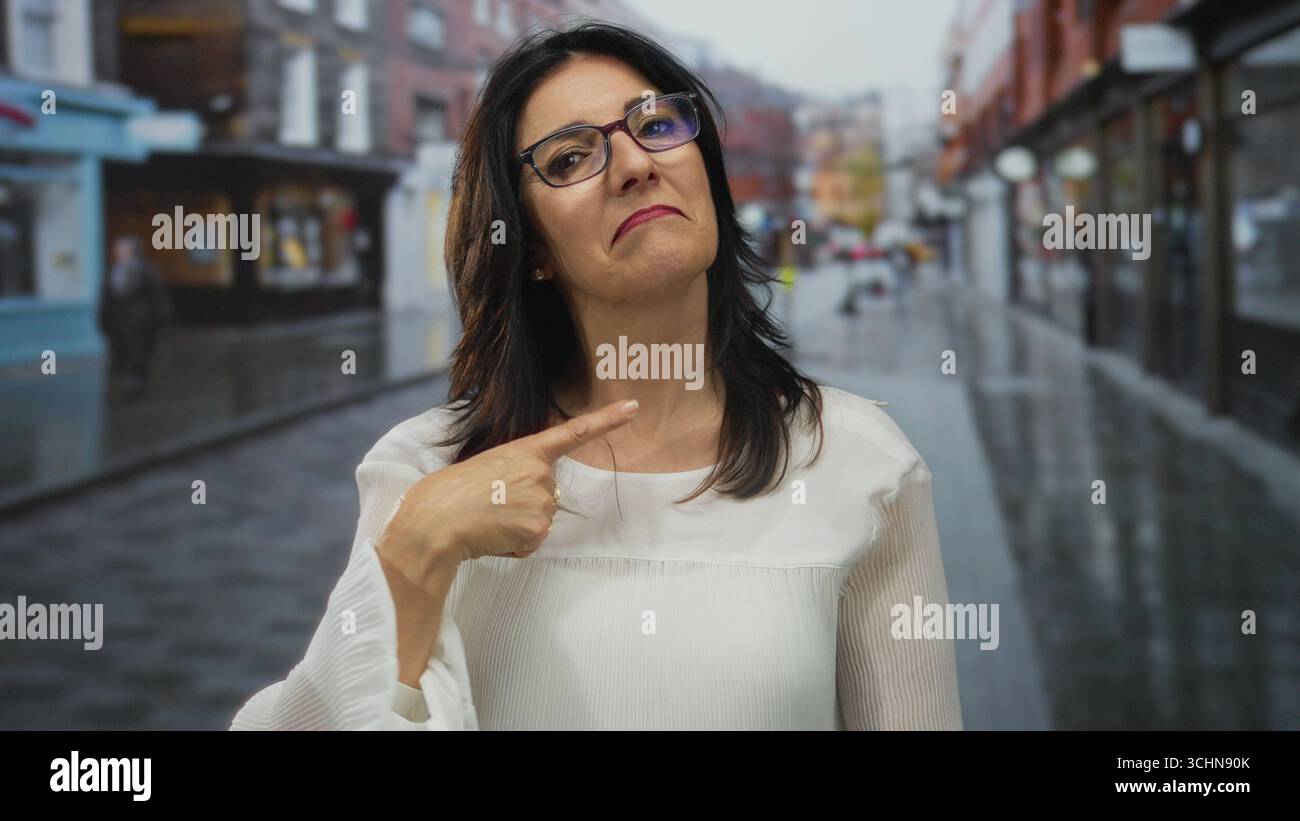 Middle aged hispanic woman points finger to chest on wet urban street ...