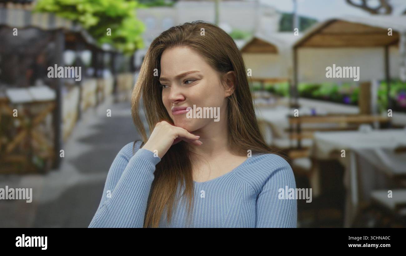 Woman touches chin with slight frown and flicks hand at outdoor ...