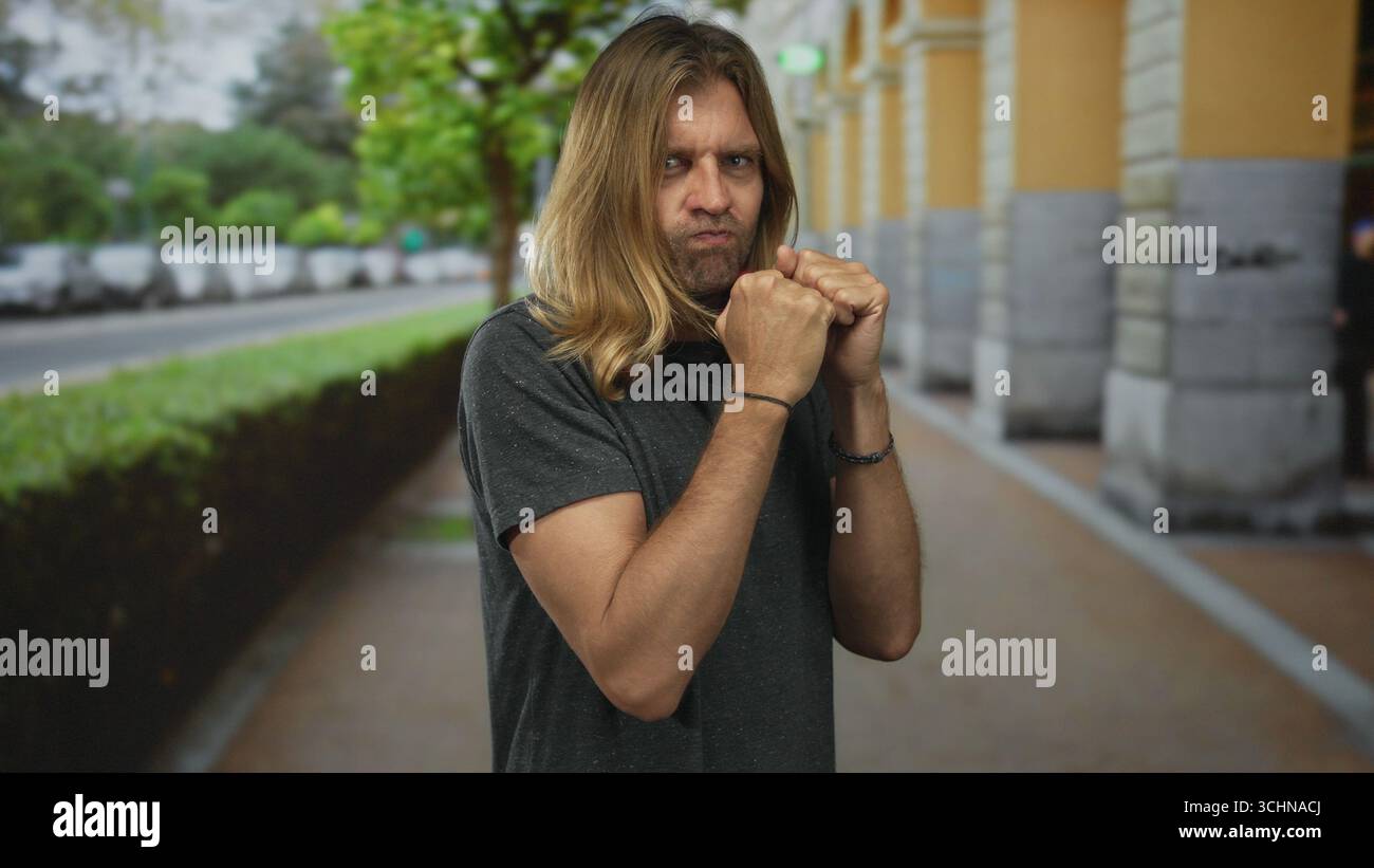 Blond man with long hair and clenched fists standing ready to punch on ...