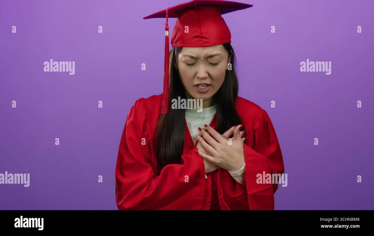 Woman wearing red graduation gown stands against a purple background ...
