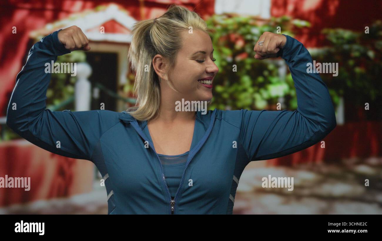 Blonde woman flexes biceps with both arms raised at house entrance ...