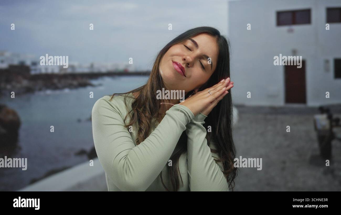 Young hispanic woman makes sleeping gesture with hands under cheek ...